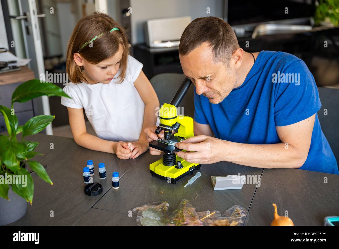 Father and daughter examining various plant samples under a microscope ...