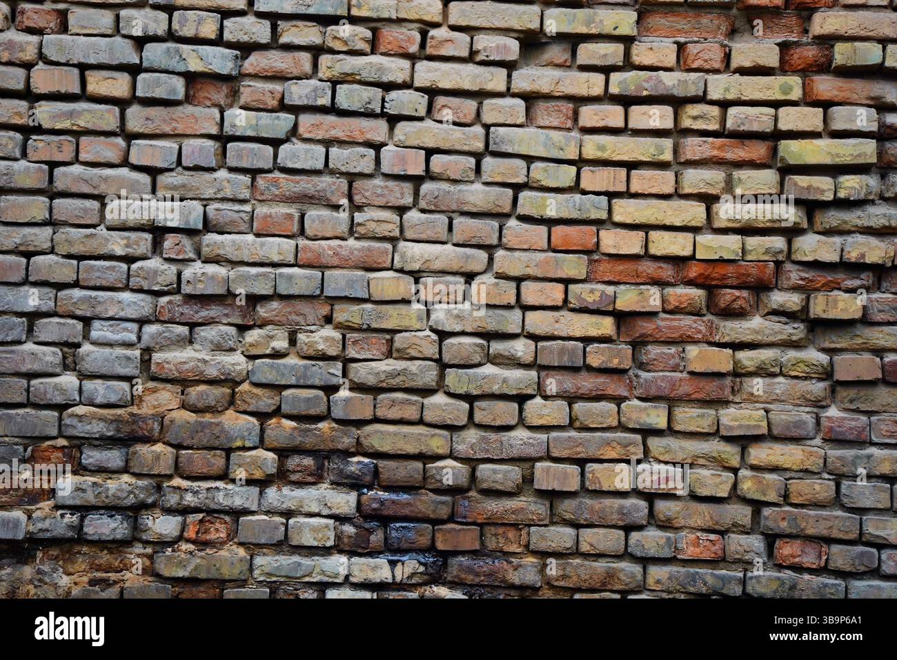 A large wall made of old bricks with dents, cracks and irregularities ...
