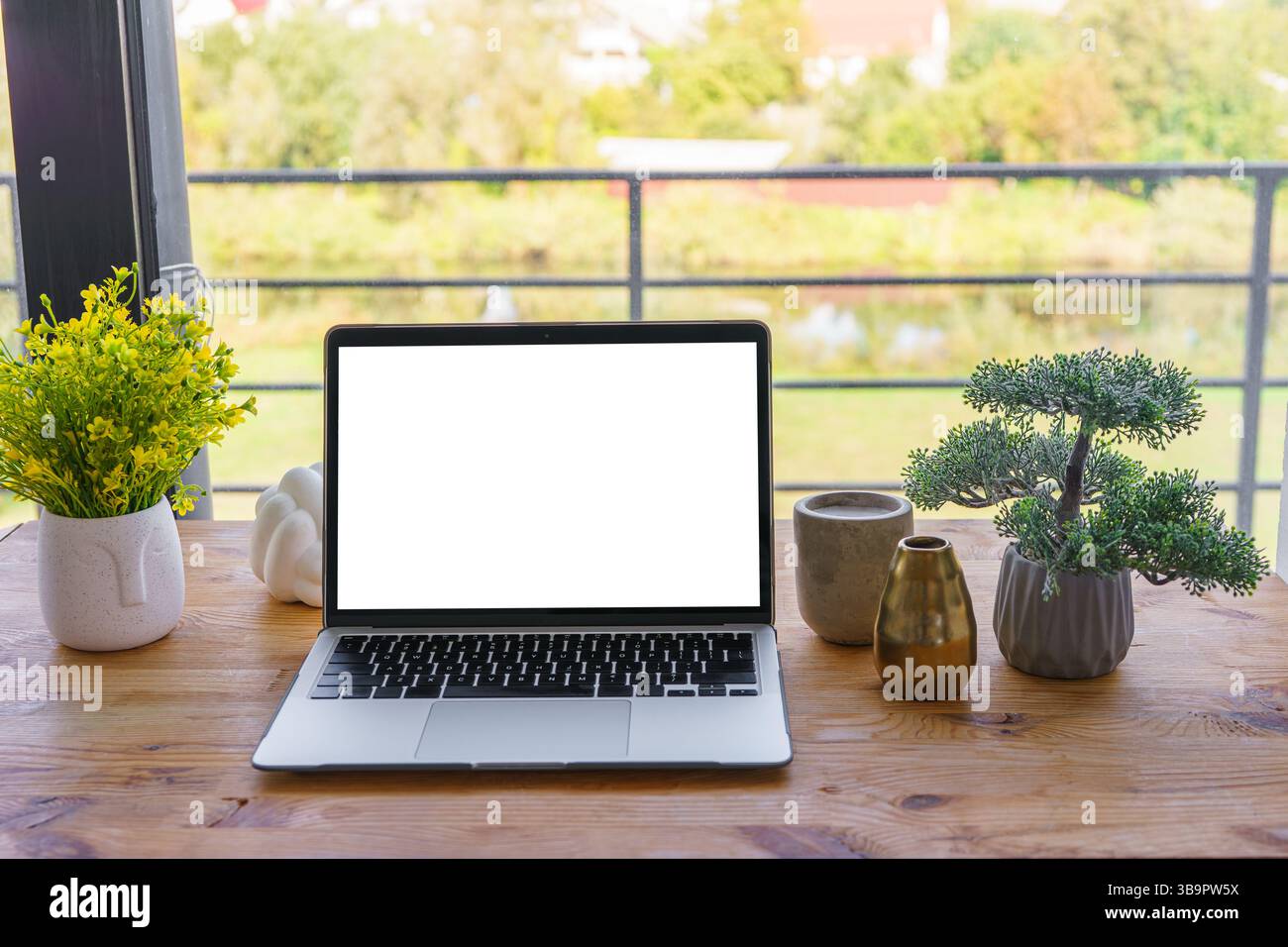 Laptop computer with white screen on wooden desk on wide window ...