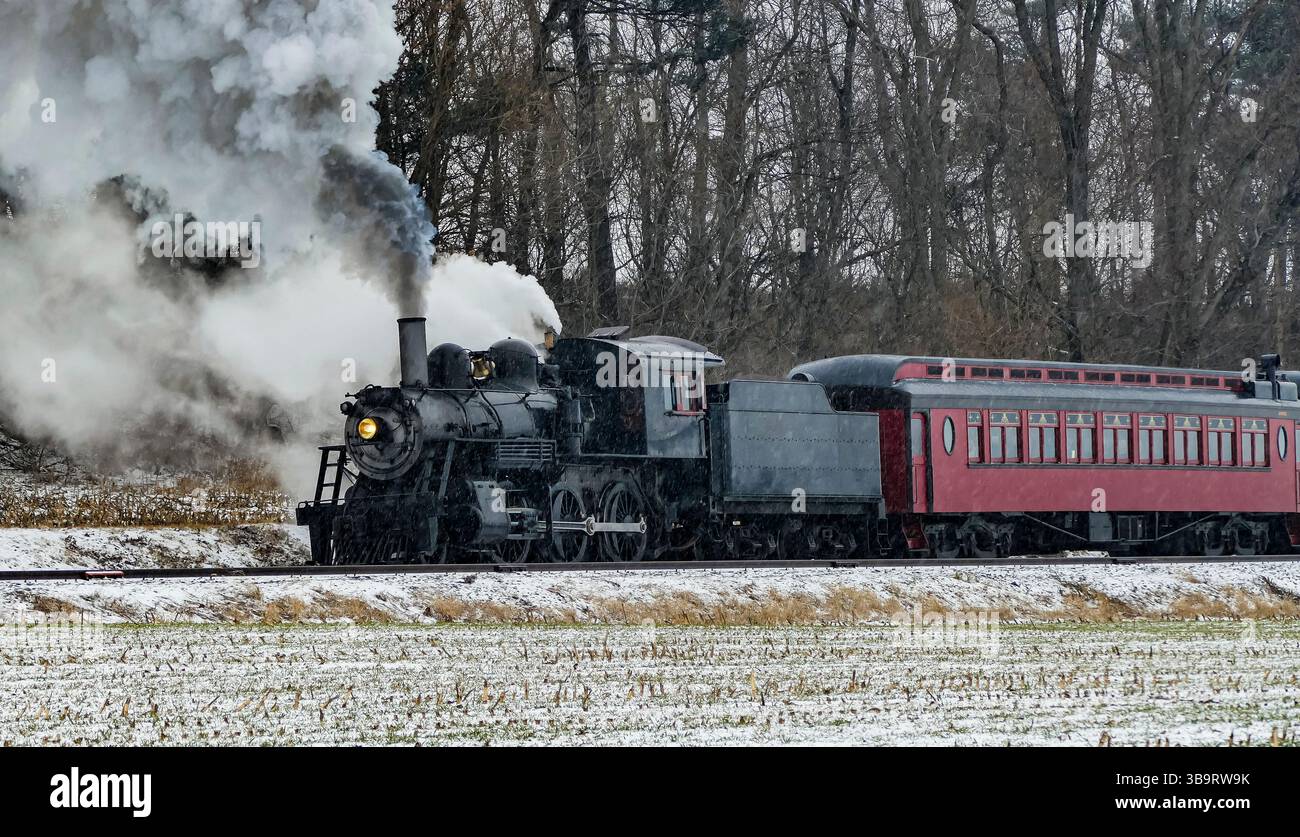 A classic steam locomotive puffs white smoke as it moves through a ...