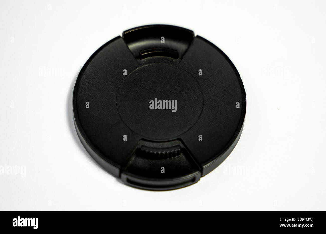 This image features a black lens cap isolated on a white surface ...
