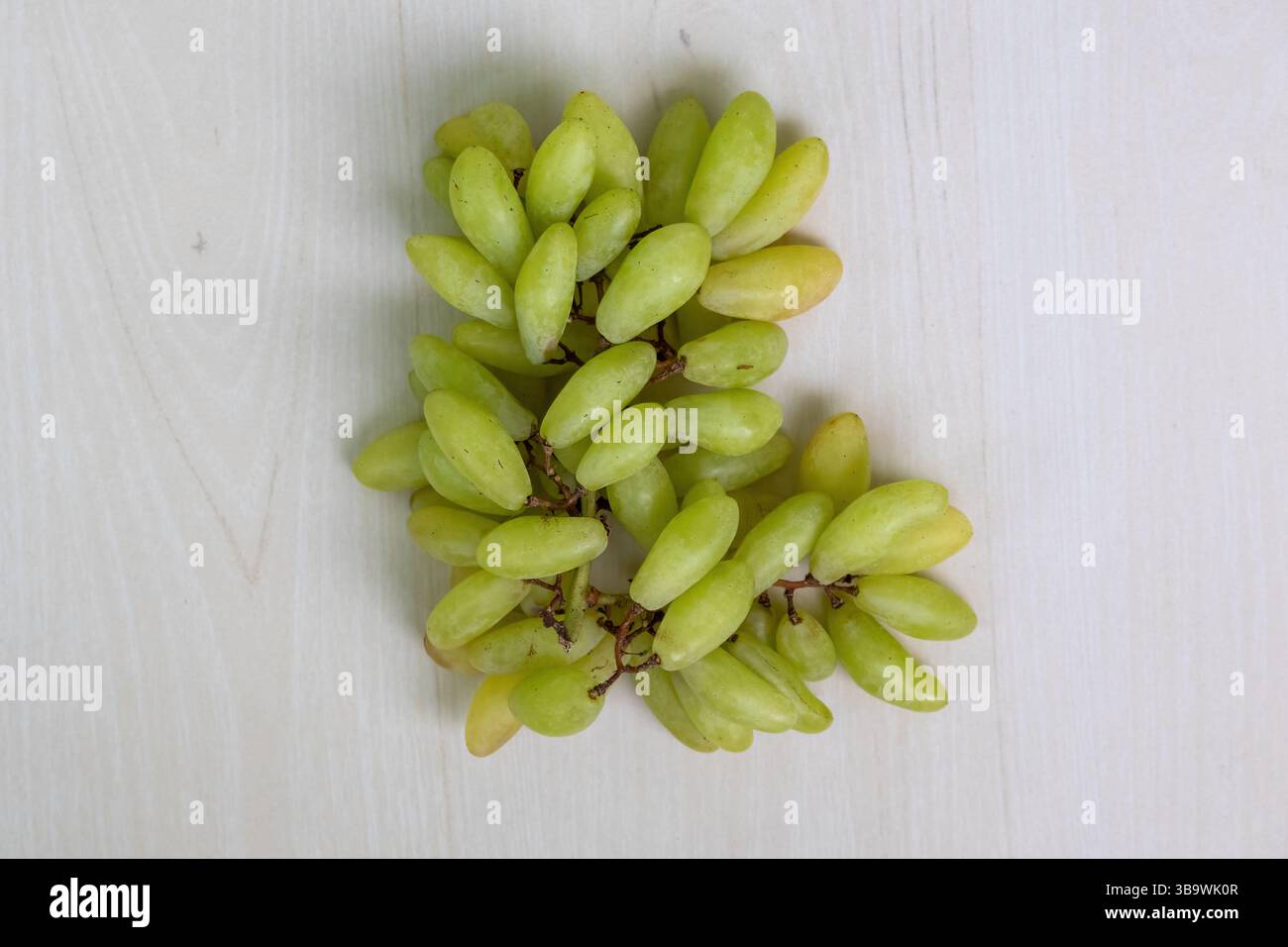 A bunch of fresh, long green grapes (Vitis vinifera) on a light wooden ...