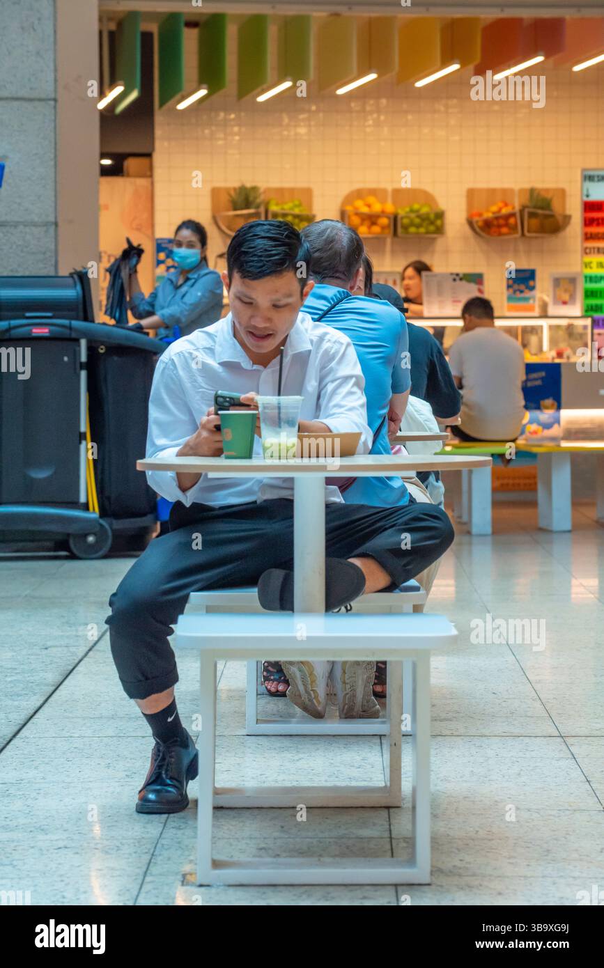 A young Asian Australian man sitting with his phone eating take away ...