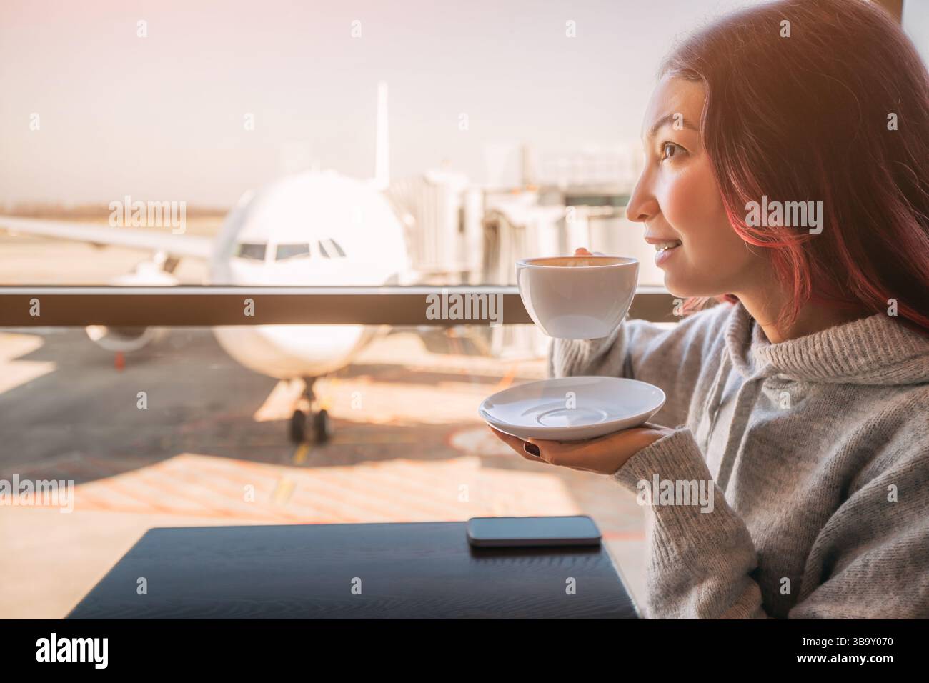 Passenger drinking coffee looking at airplane through window at airport ...