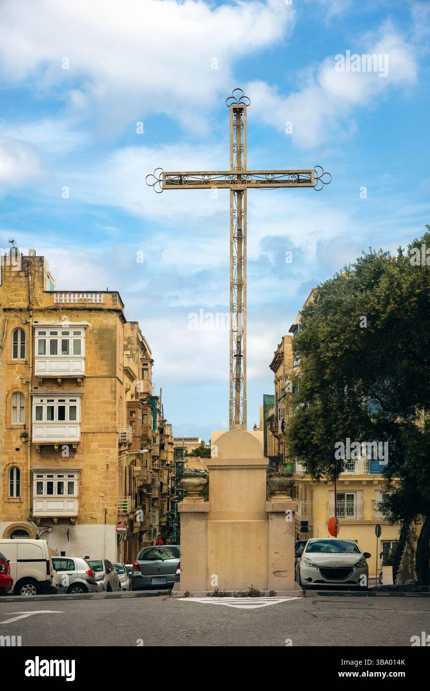A tall wrought iron cross on a stone pedestal at a crossroads in a ...