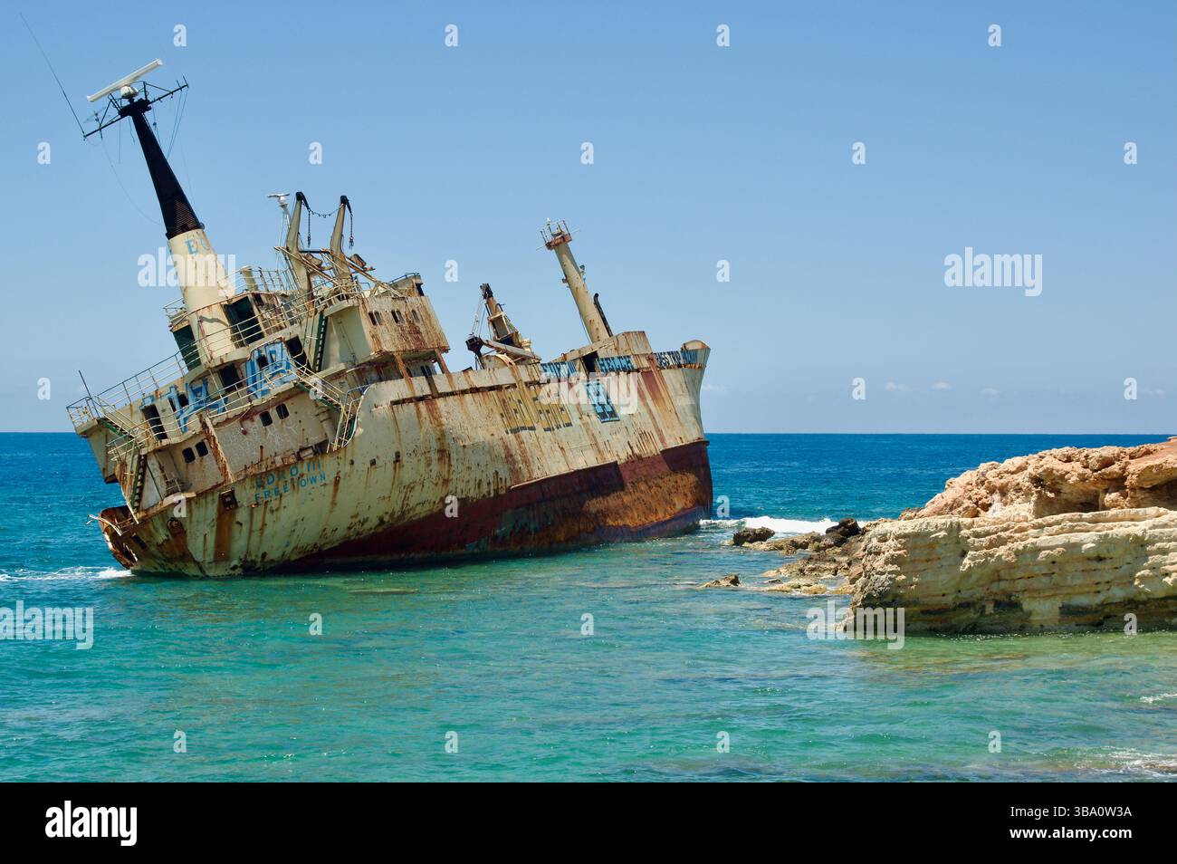 Shipwreck resting on a rocky coastline under a bright blue sky with ...