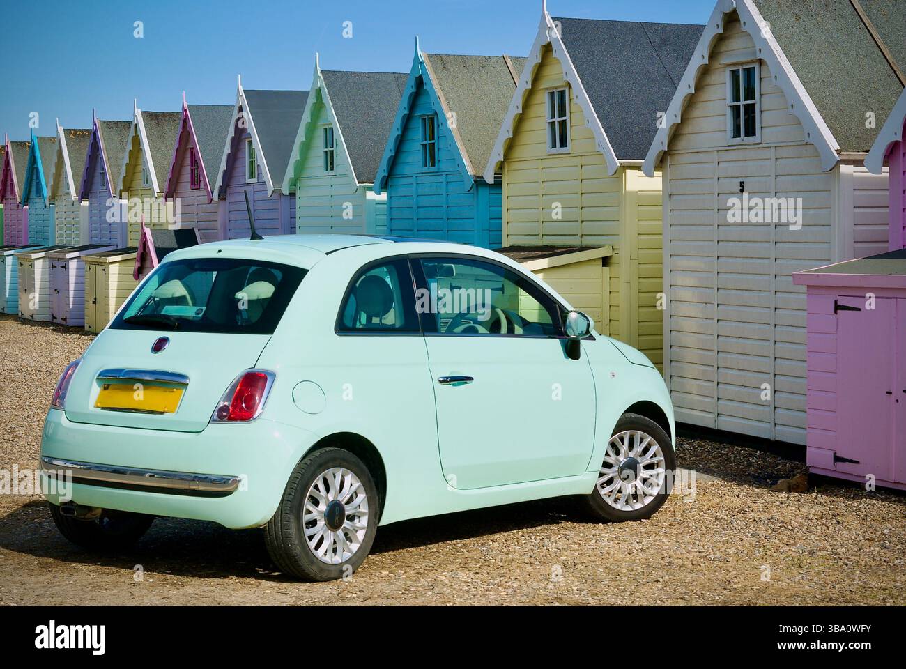 A light blue compact car parked by a row of colorful beach huts under a ...