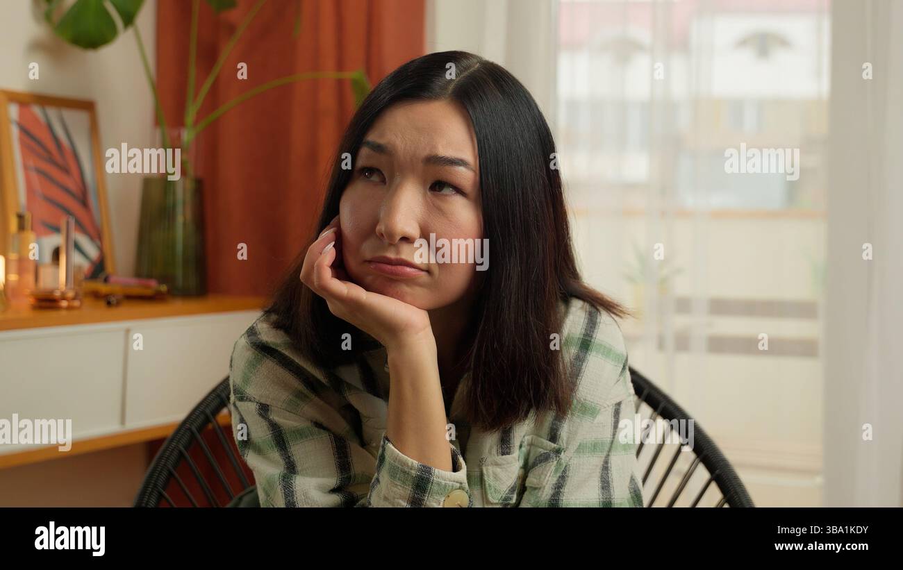 Pensive thoughtful Asian Korean Chinese Japanese woman thinking at home ...