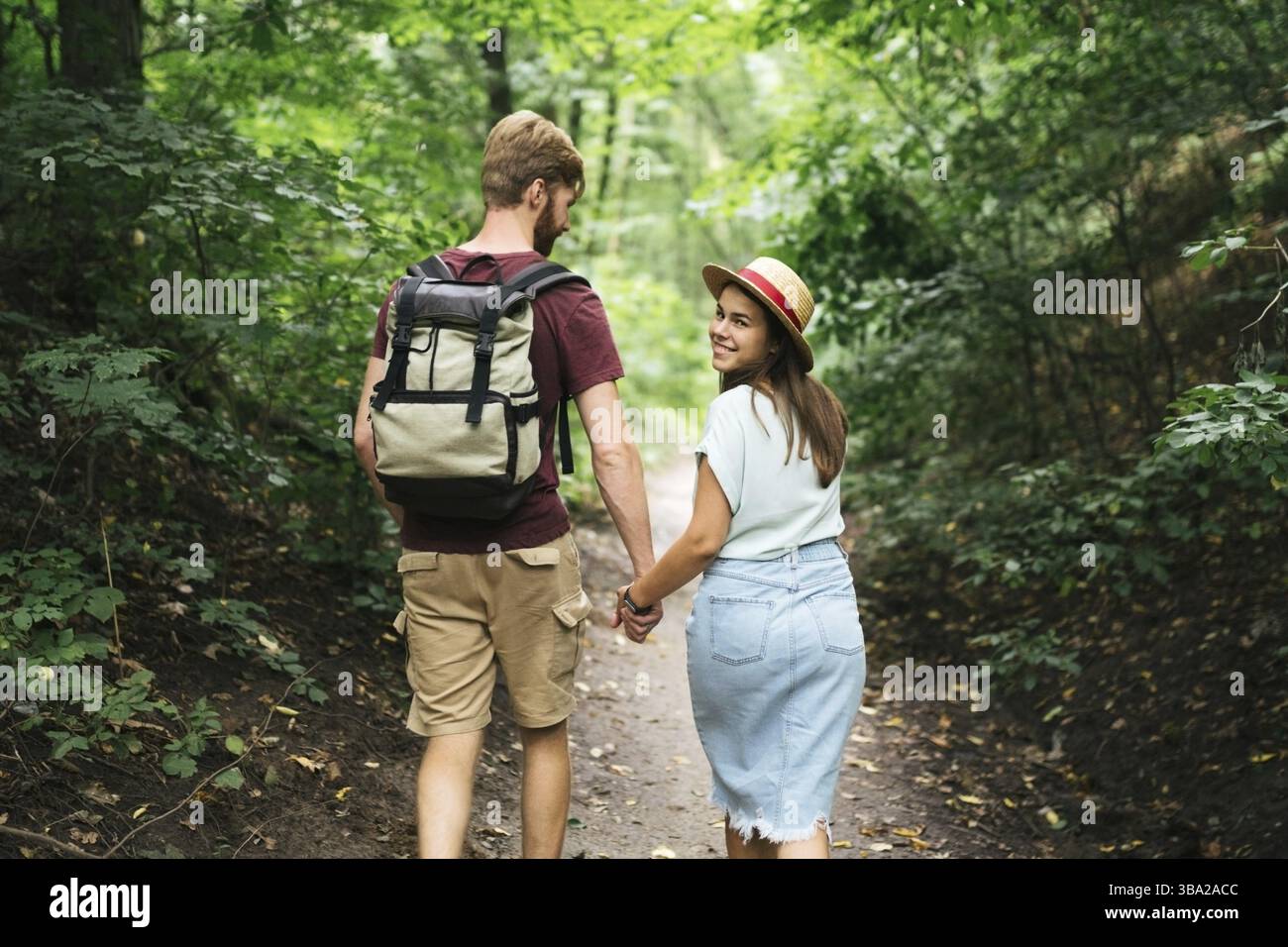 Guy and girl walk together in wood along the trail, holding hands. Back ...