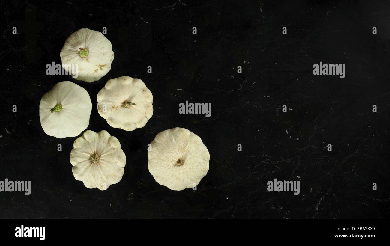 Five white pattypan squash heads on dark marble like board, wide banner ...