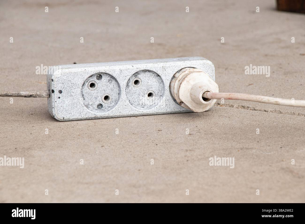 An outdoor extension cord with three sockets, white with black paint ...