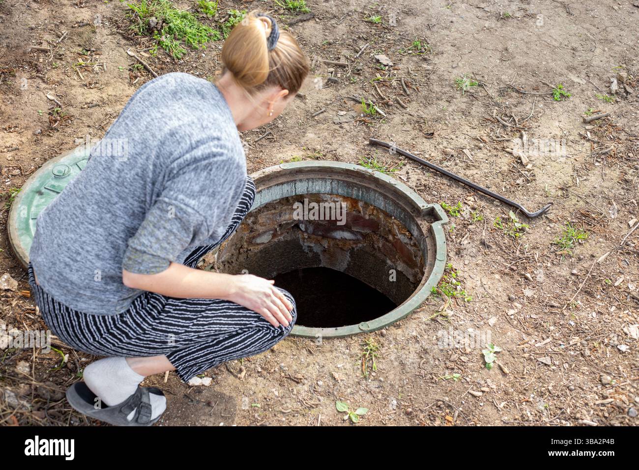 A woman looks into an open septic tank to check the level of sewer ...