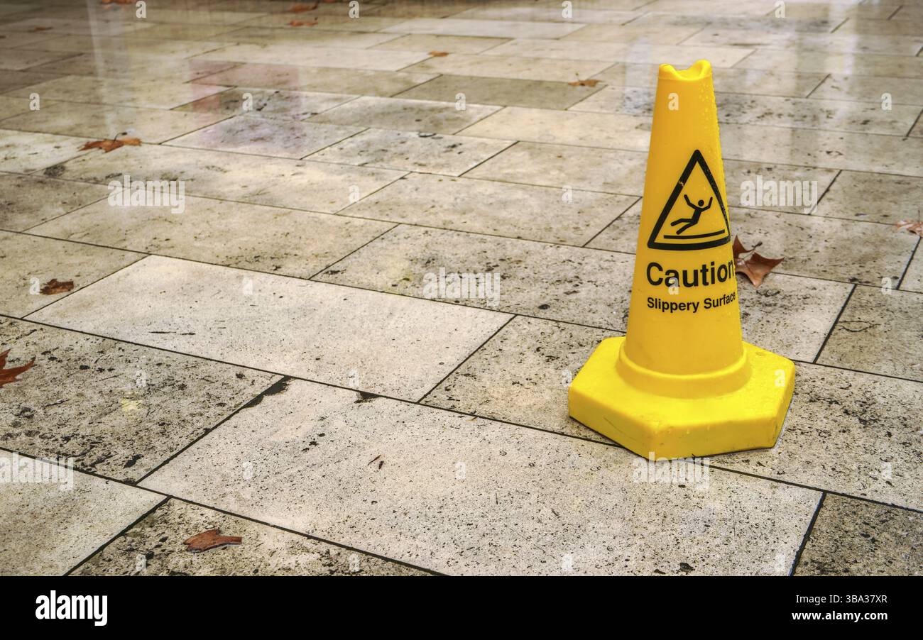 Yellow cone with caution slippery surface sign, on wet pavement tiles ...
