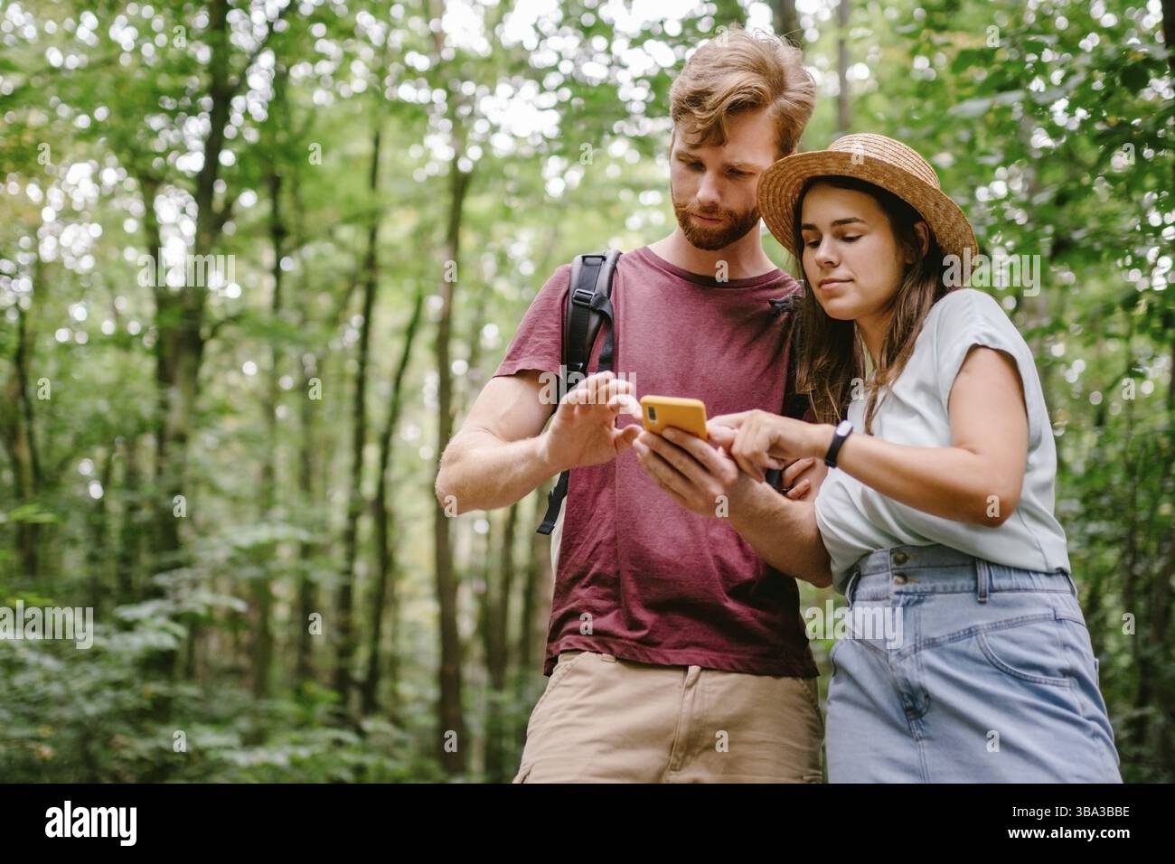 Hikers using mobile gps for directions. Happy couple checking smartphone in the woods during ...