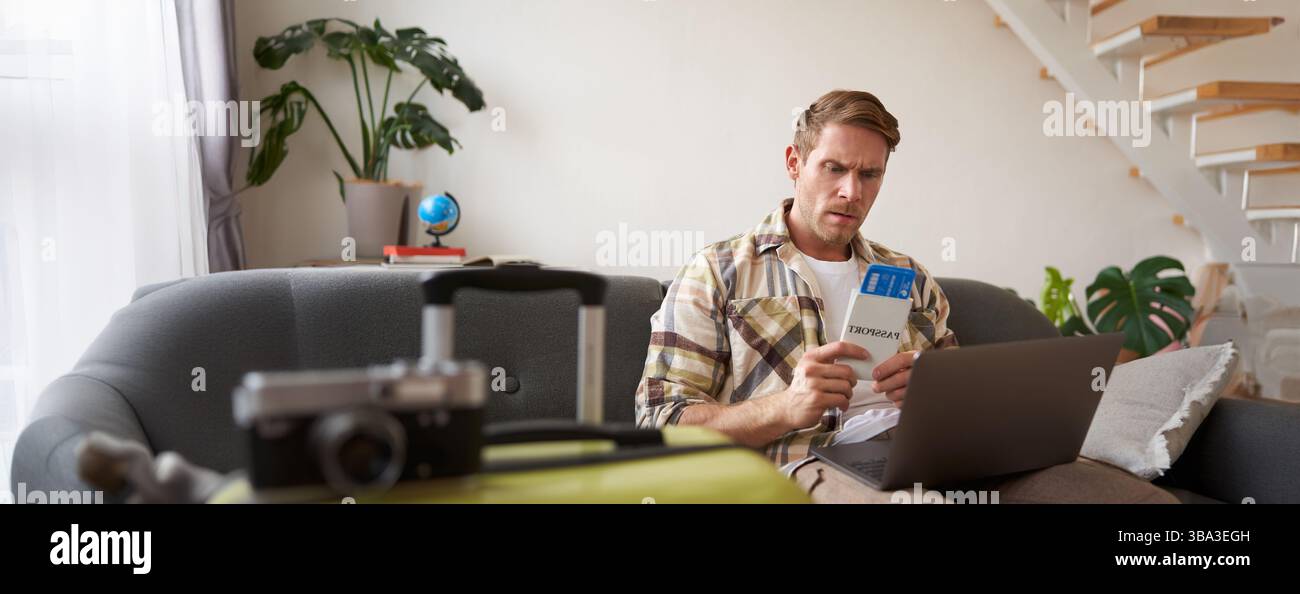 Portrait of grumpy man, holding tickets and passport, has laptop opened ...