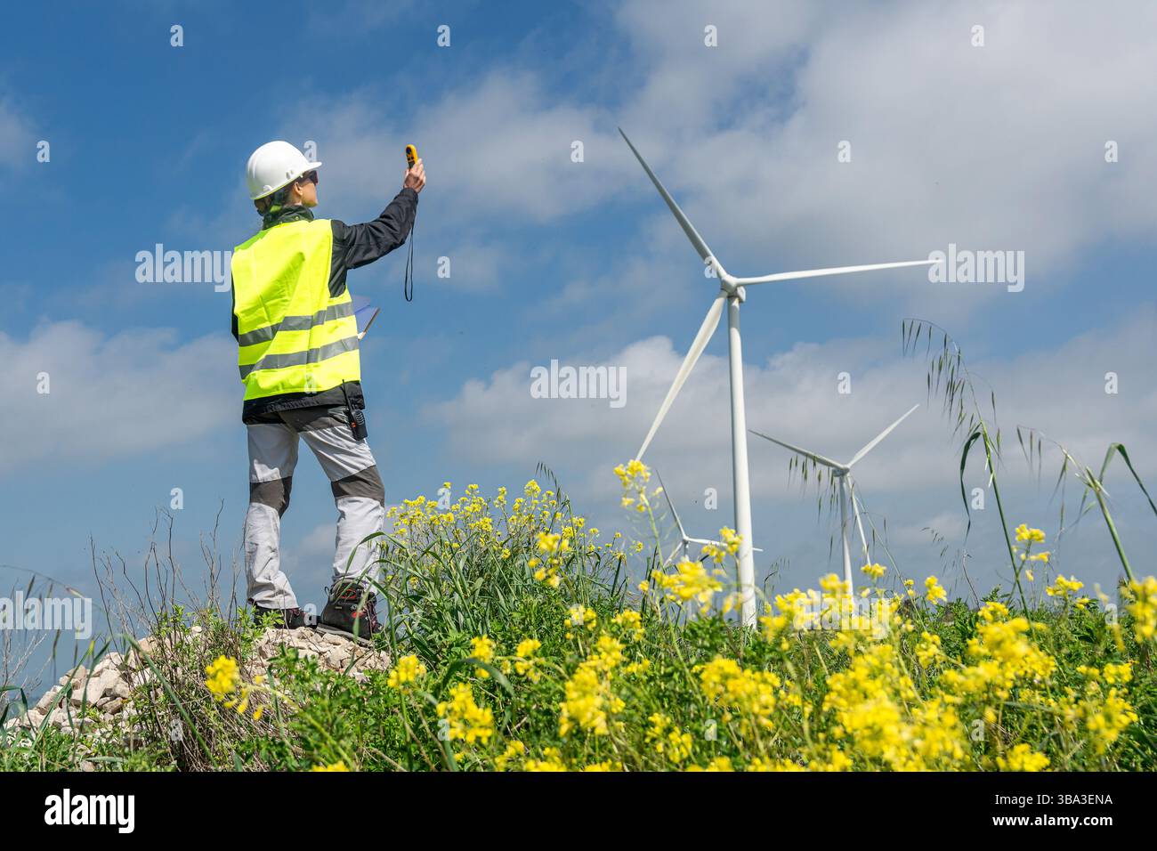 Engineer measuring wind turbine efficiency with anemometer in field of ...