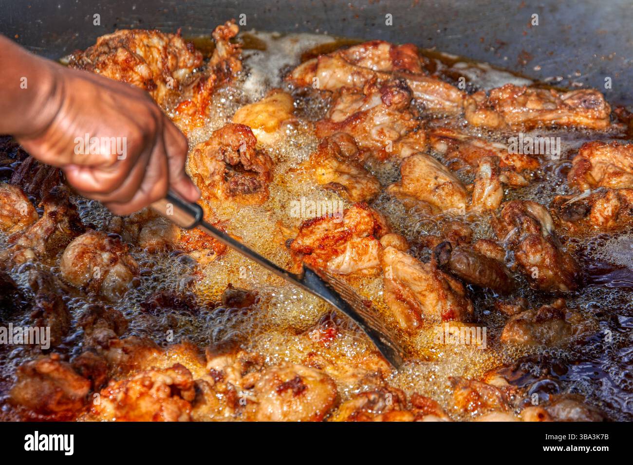 deep frying chicken boiling in oil, african american indian hand mixing ...