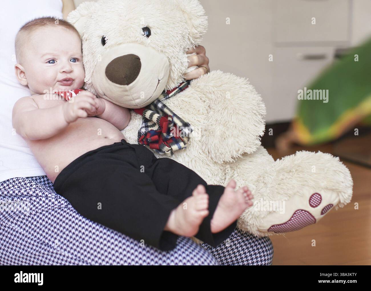 Four months old baby boy sitting on her mother knees, large plush teddy ...
