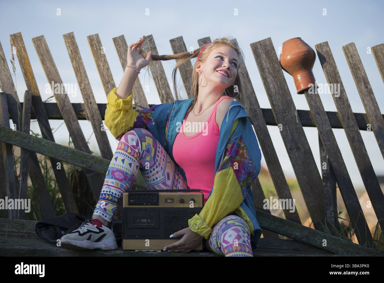 A beautiful country girl in bright clothes sits on a wooden bench with ...
