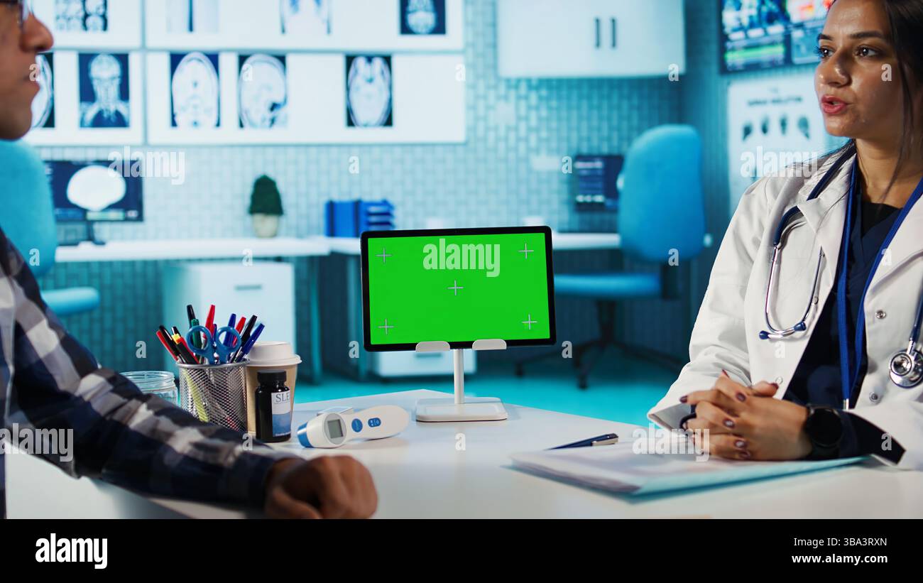 Indian physician consulting male patient in medical facility next to chroma key, using ...