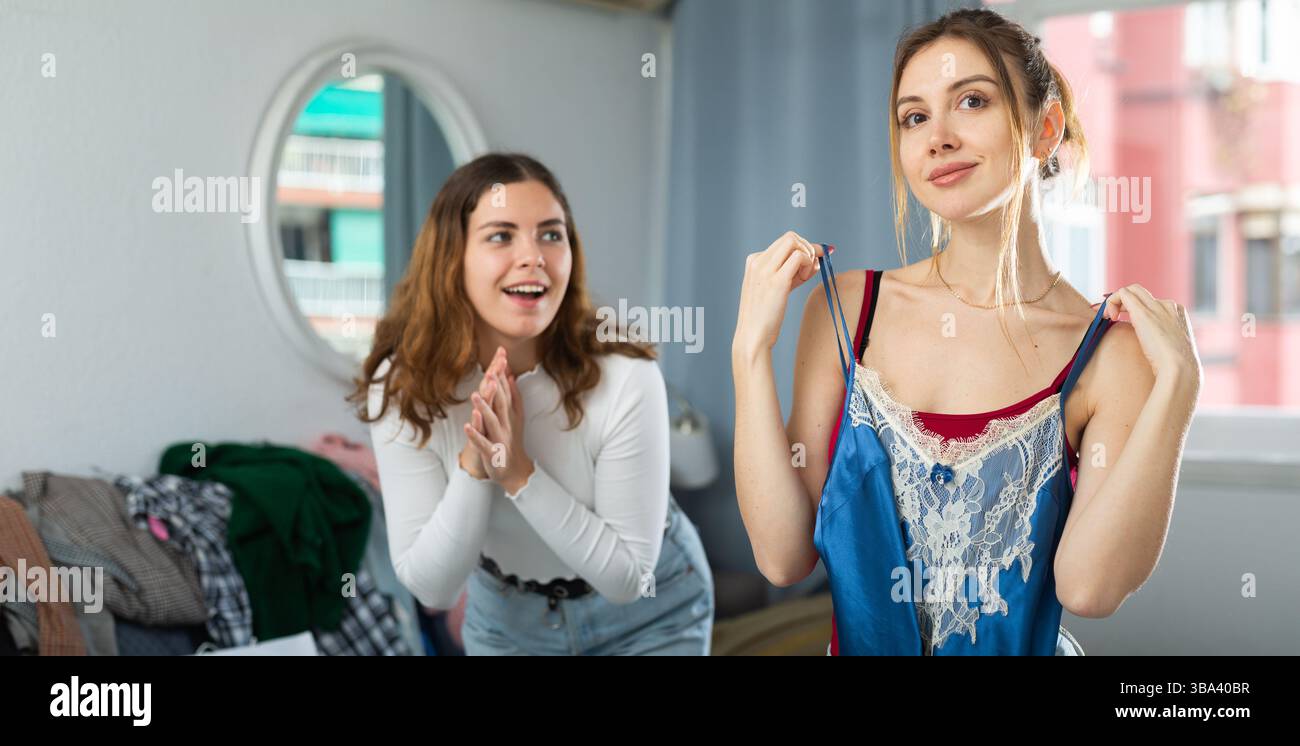 Two girls talking and showing each other clothes in home interior Stock ...