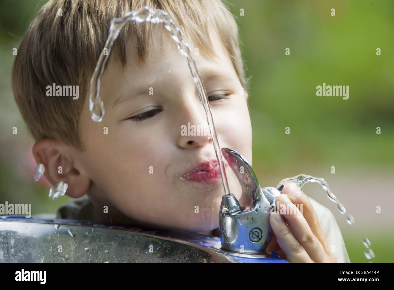 A child drinks water from a fountain. A jet of water and a drinking man ...