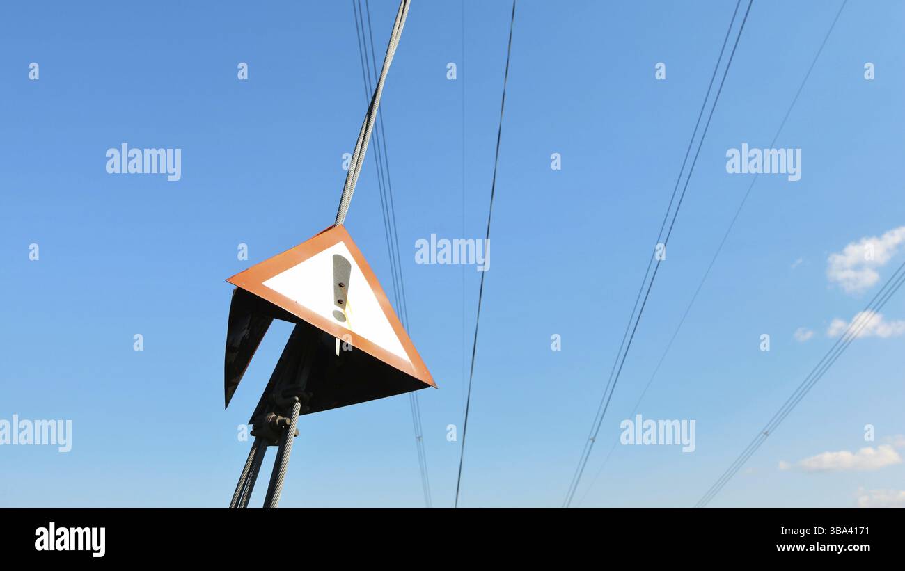 Red triangle with exclamation mark on steel cable of electric pylon ...
