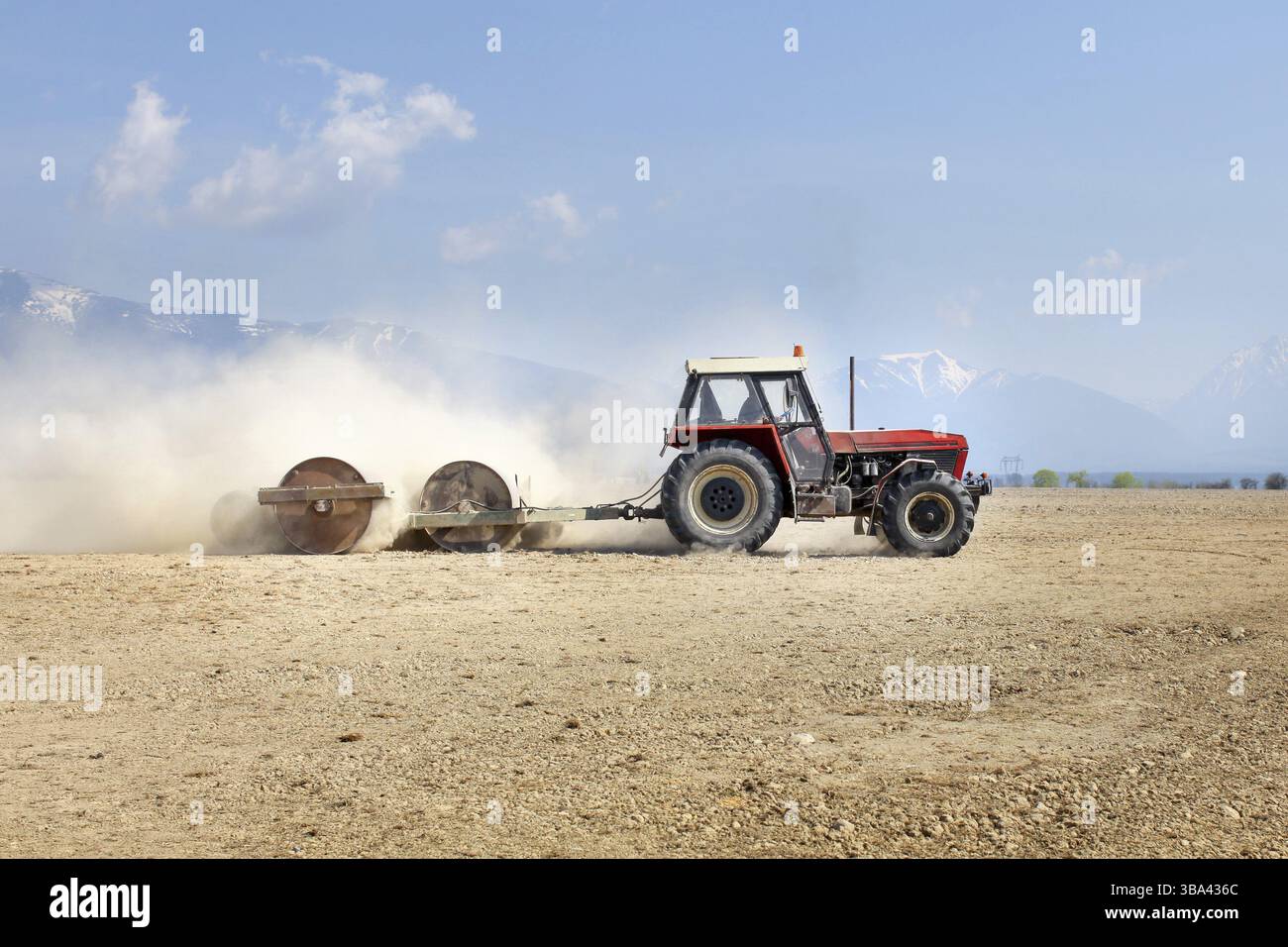 Tractor pulling heavy metal rollers, preparing field in spring, with ...