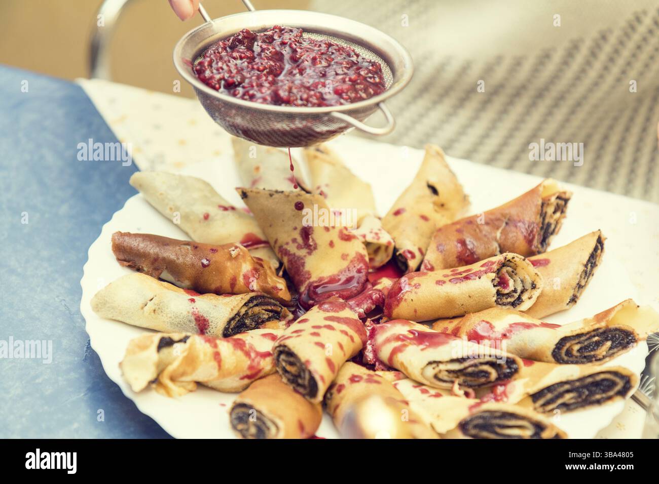 Crepes filled with poppy on white plate. Spring rolls. Woman pouring ...