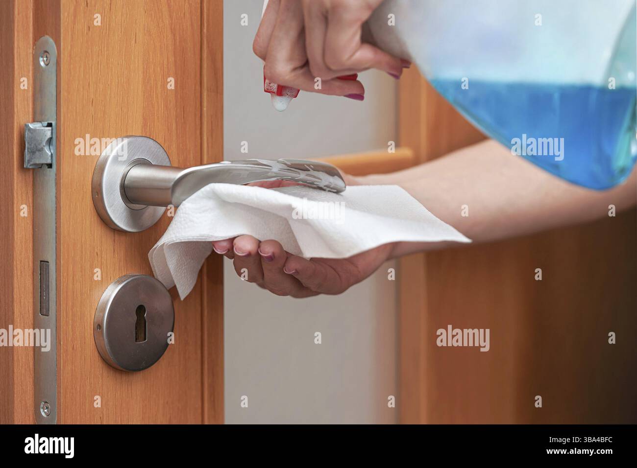 Hand cleaning metal door handle with paper tissue towel, spraying ...