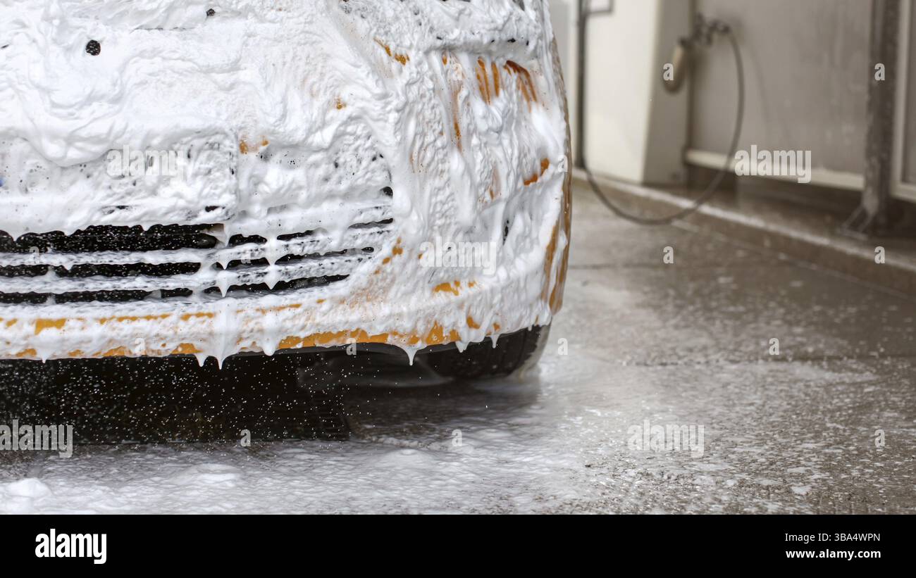 Front bumper of yellow car being washed in carwash, completely covered ...