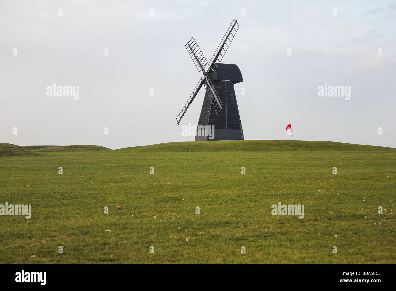 Windmill and red flag with green lawn and overcast sky in Rottingdean ...