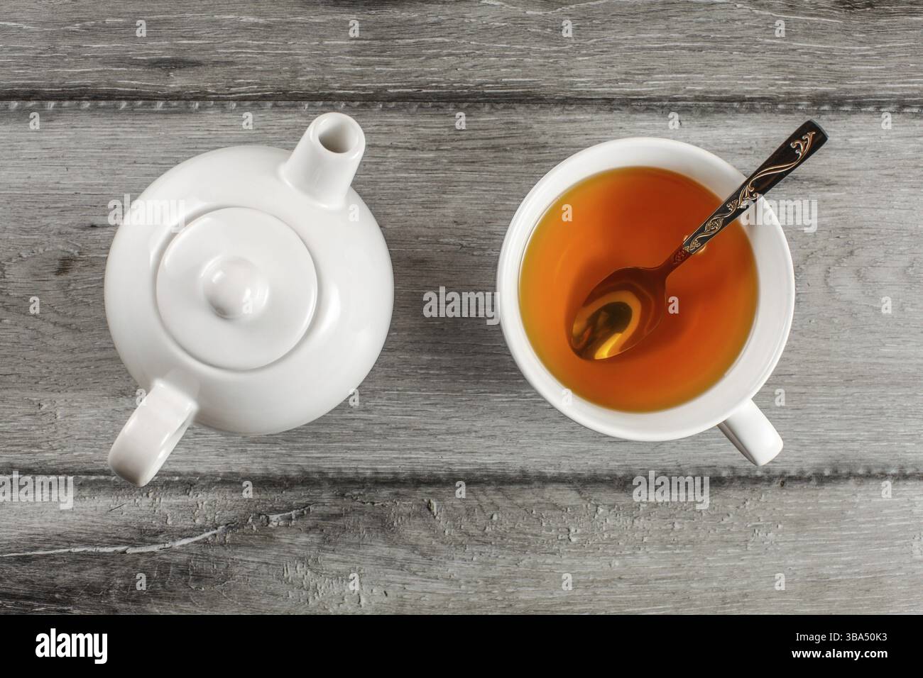 Table top view on small white teapot and cup full of hot amber tea with ...