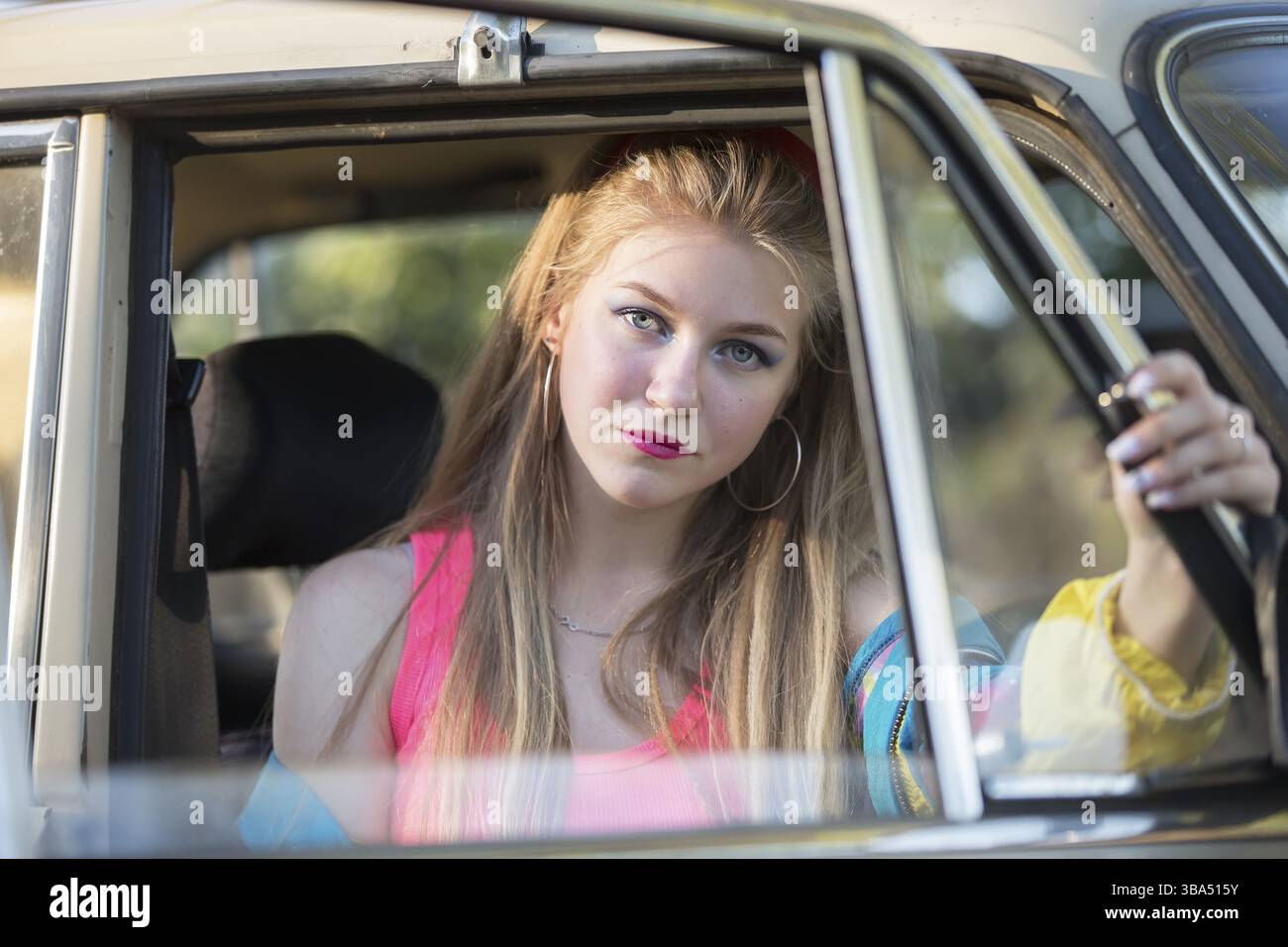 A beautiful blonde girl with long hair looks out of the car window ...