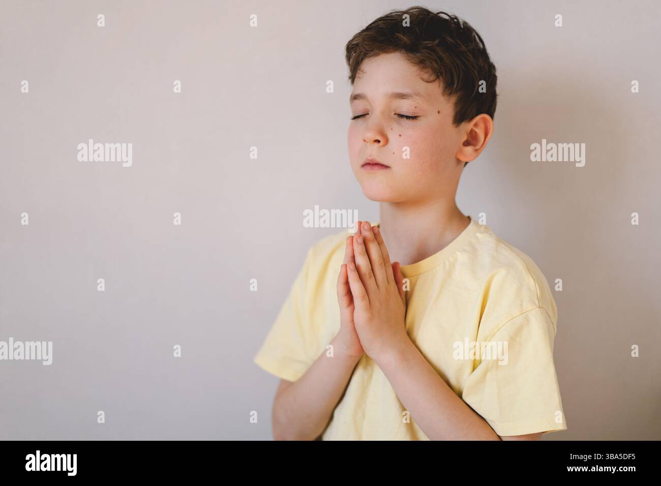 A boy with folded hands in front of him, he prays in his room Stock ...