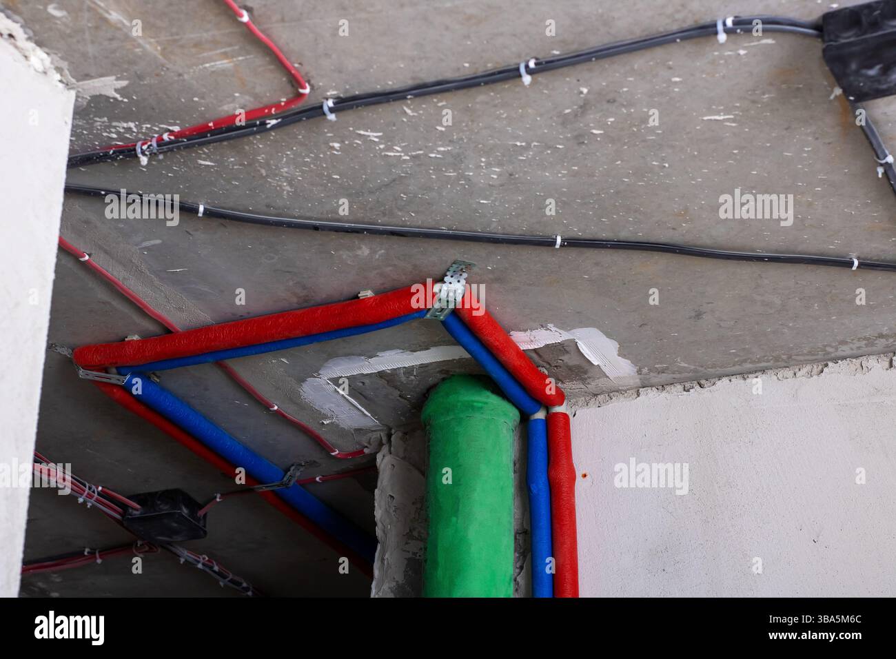 A green pipe is carefully surrounded by vibrant red and blue wires that ...