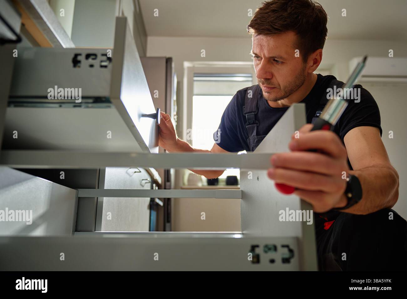 Man assembling kitchen drawer in modern cabinet using screwdriver ...