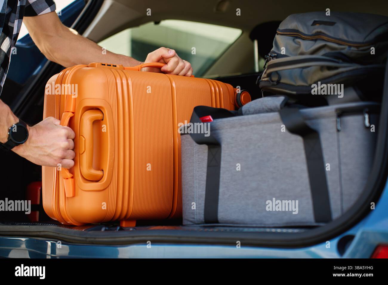 Man loading orange suitcase into car trunk before journey. Packing ...