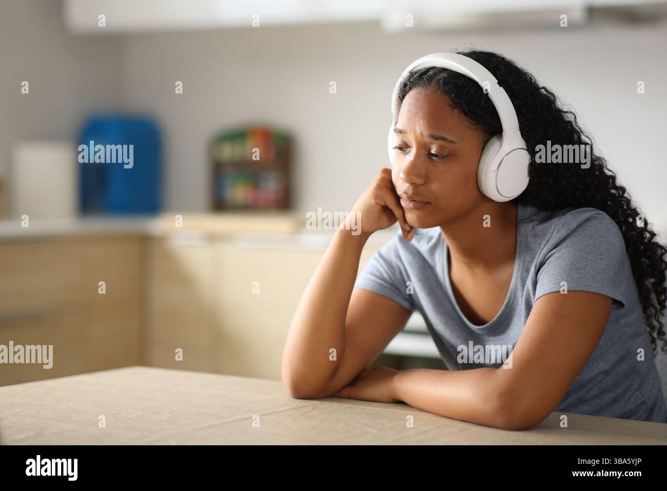 Sad black woman wearing headphone listening audio in the kitchen at ...
