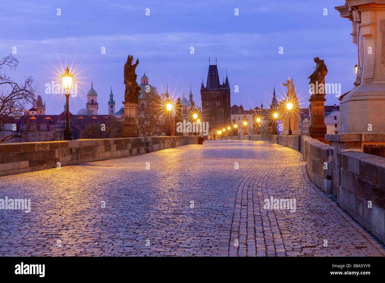 Charles Bridge in Prague, Czech Republic, illuminated at dawn with statues and historic towers ...