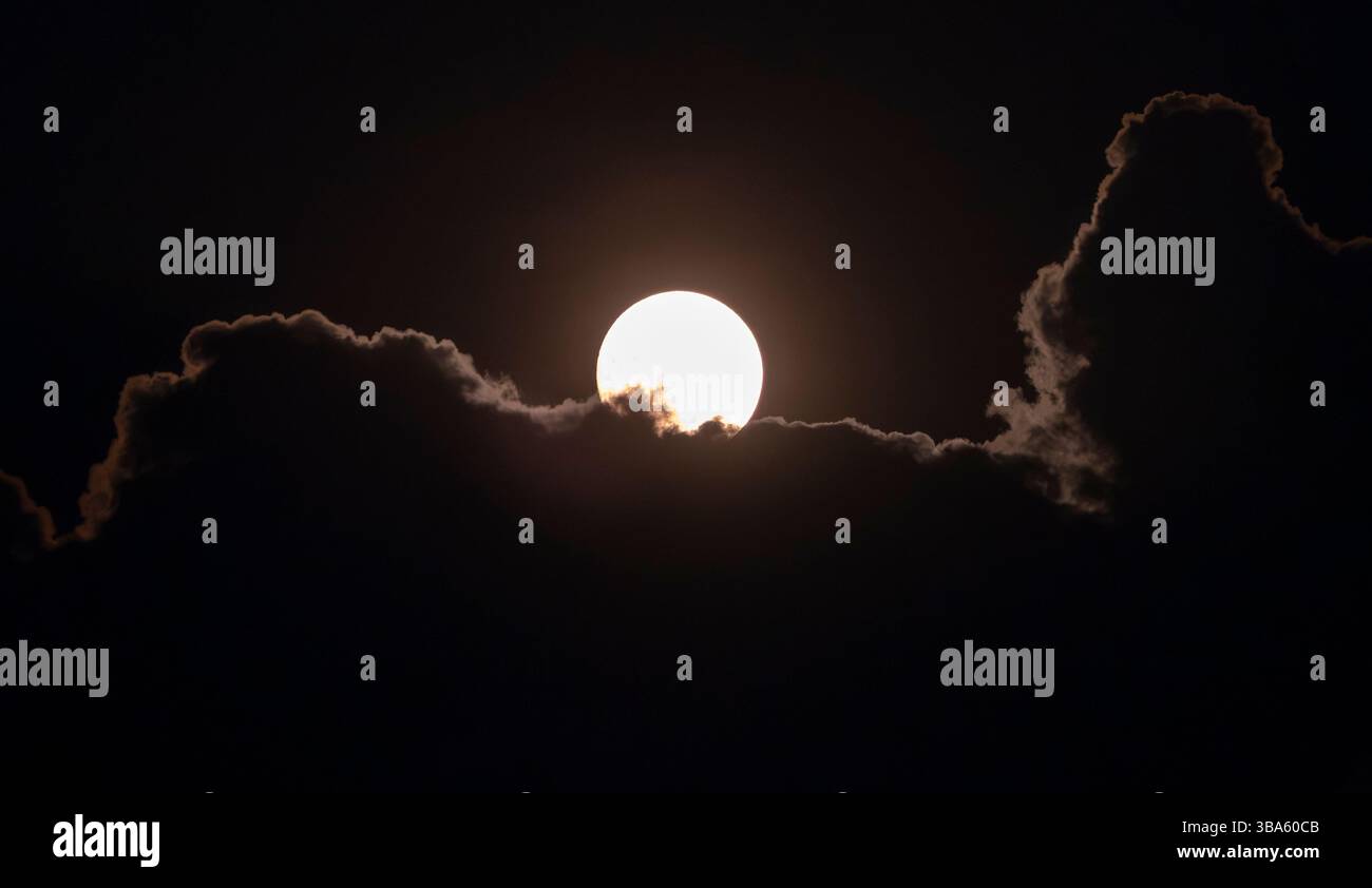 A bright full moon lights up the passing clouds on a Spring evening ...