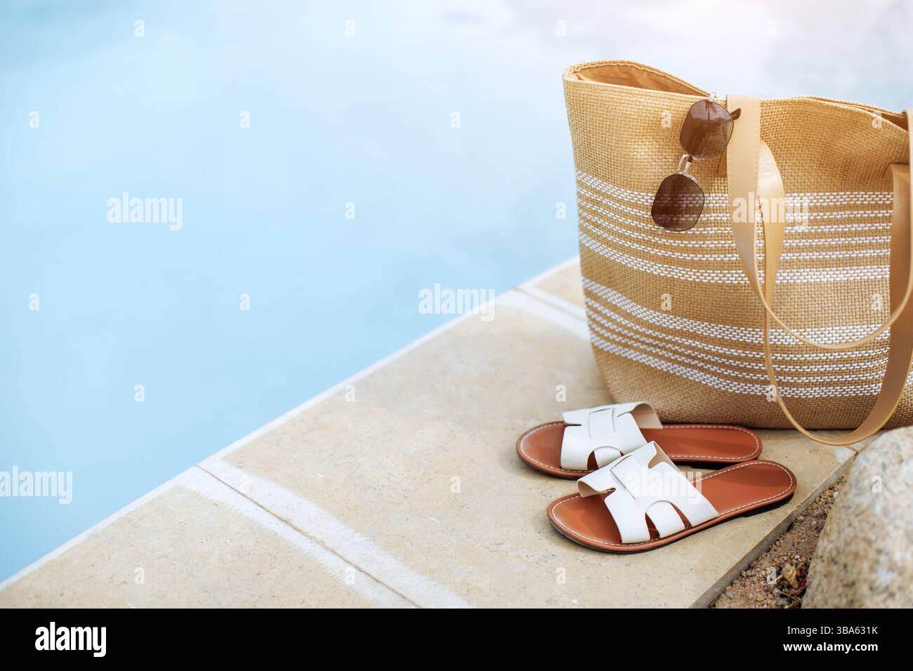 Vacation Concept. Straw beach bag with white sandals placed by swimming ...