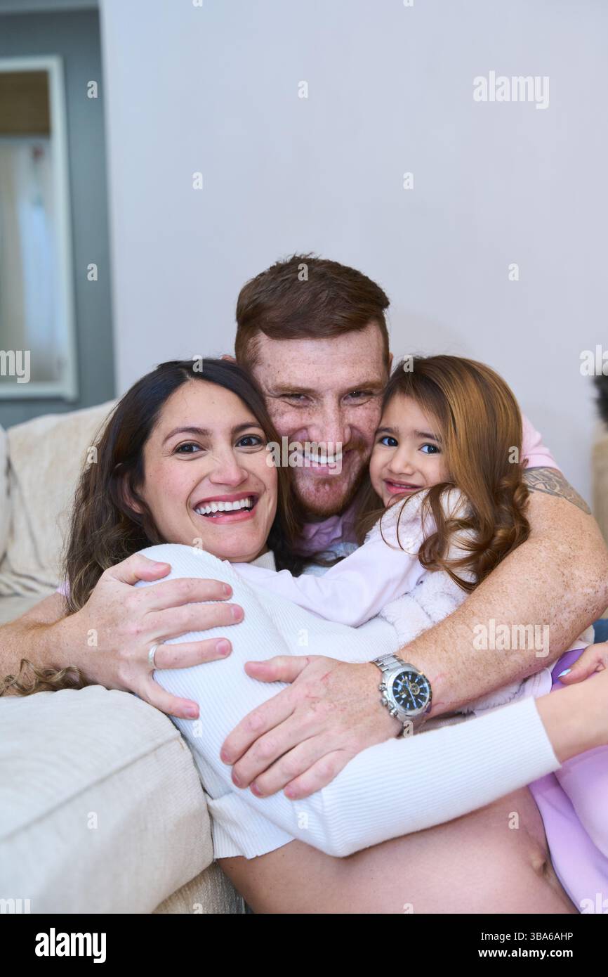 Happy latin family embracing on a sofa, with pregnant mother, father ...
