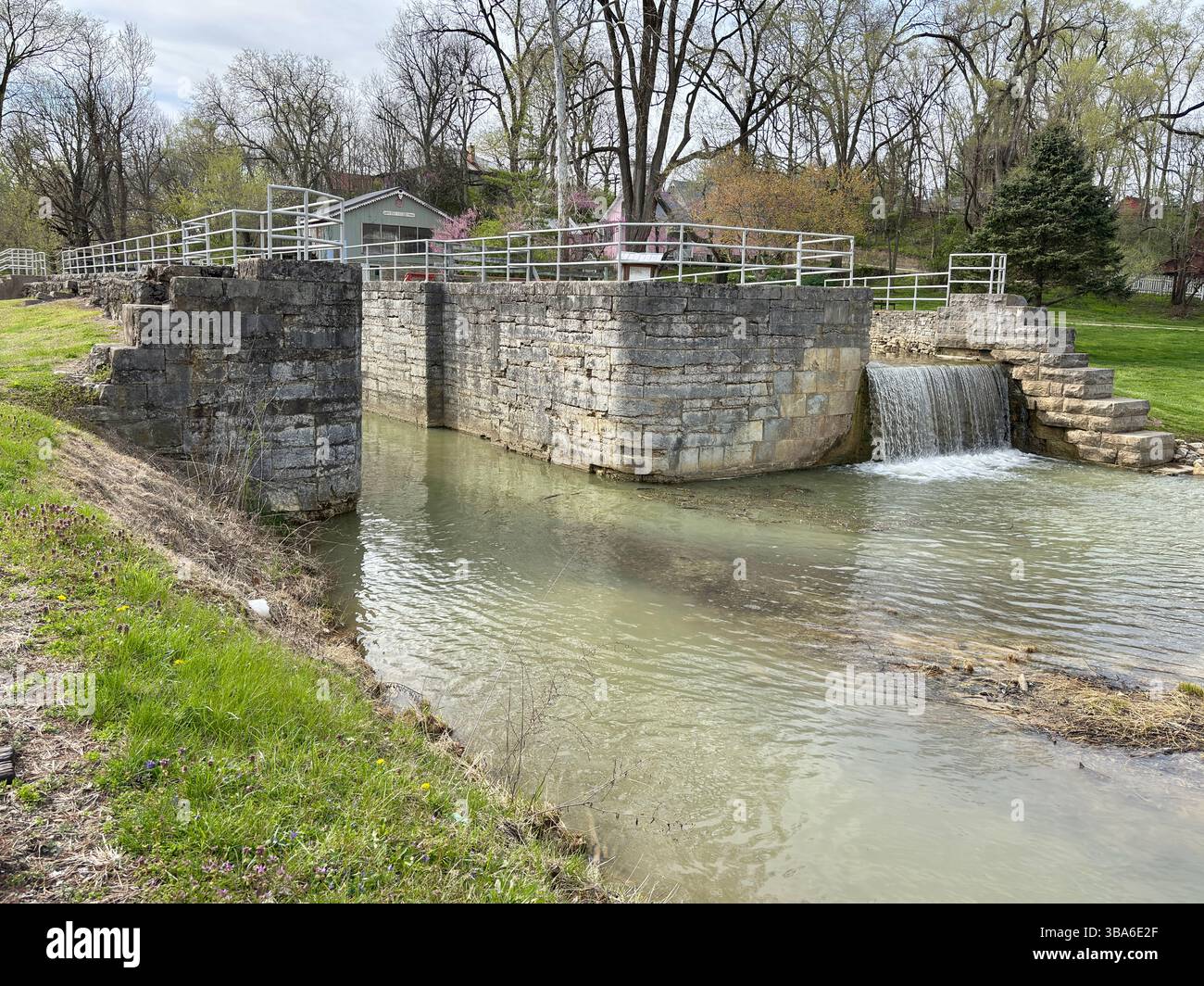 Historic stone canal lock with flowing waterfall in small town park ...