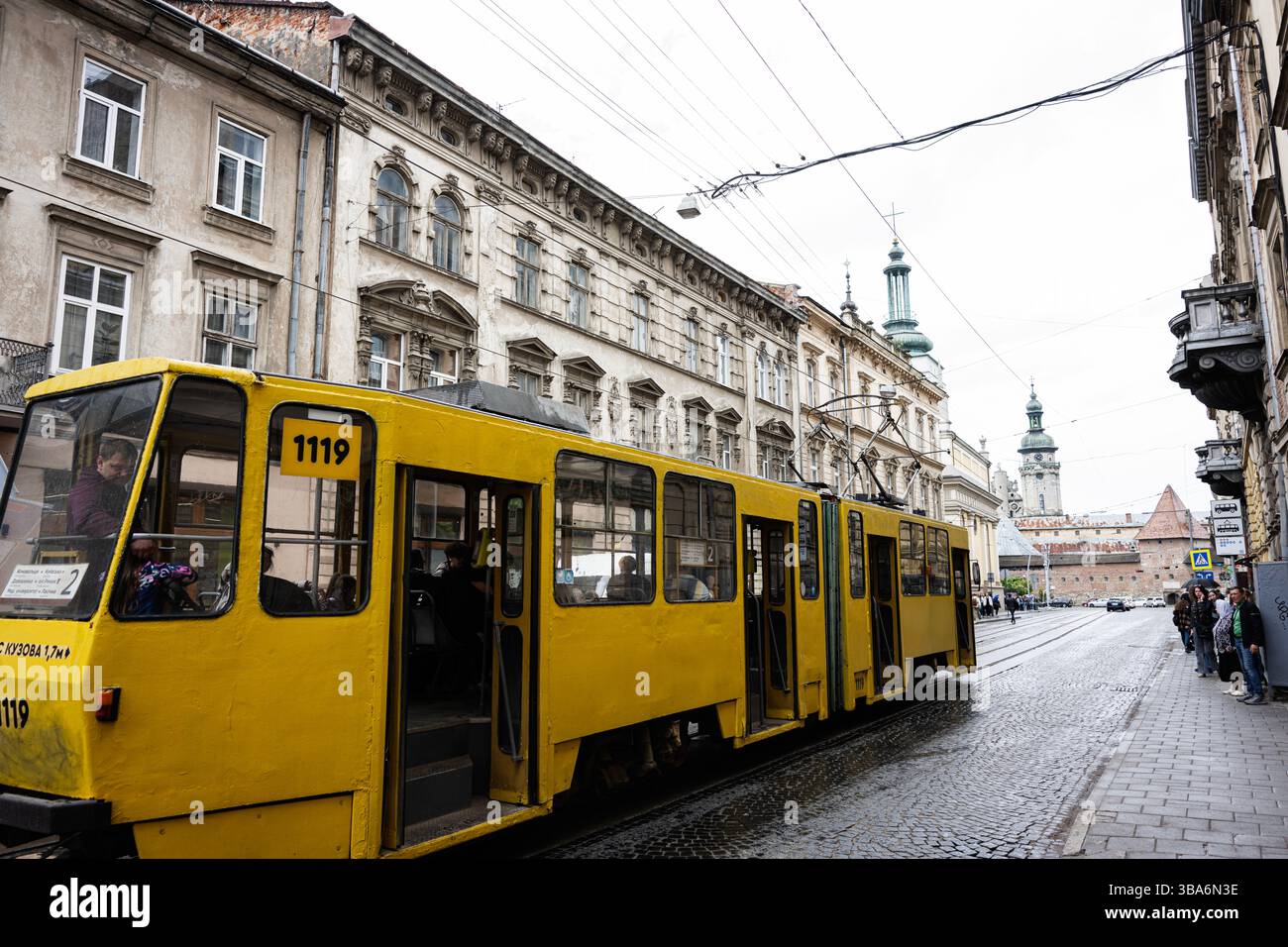 Lviv, Ukraine - May 04, 2025: A yellow tram moves along a street lined ...
