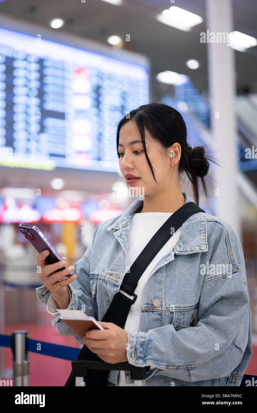 A positive, thoughtful Asian female passenger checks her flight ...