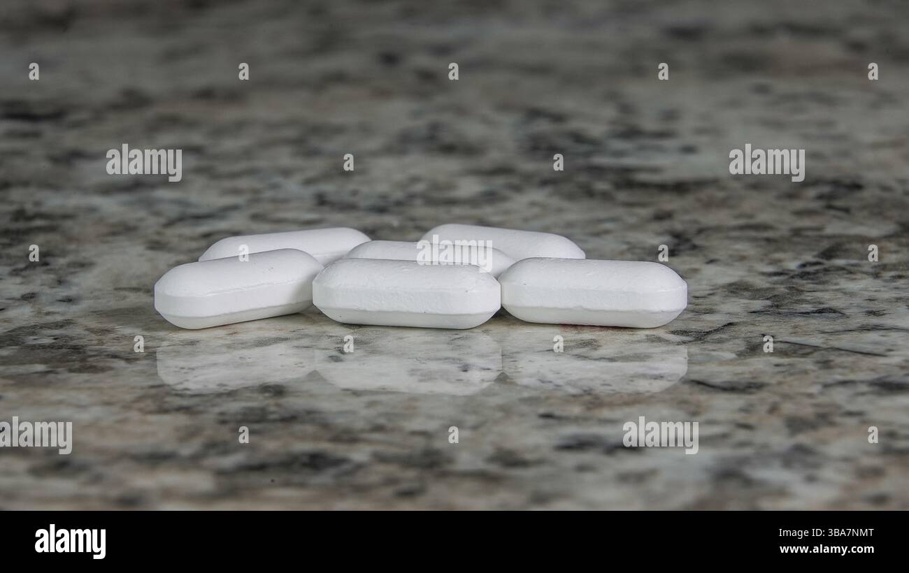 Six white pills are scattered on a light colored stone countertop ...