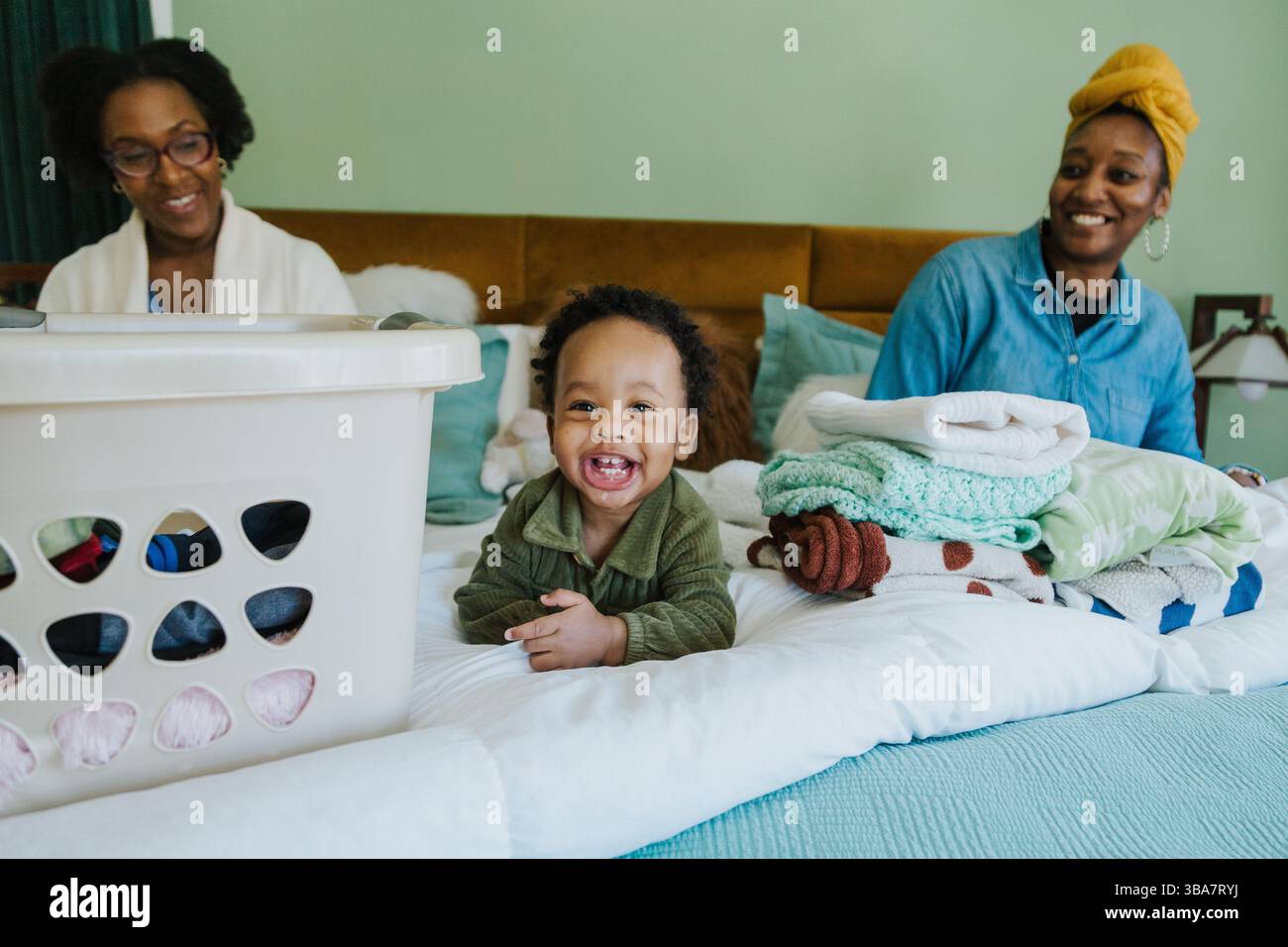 Black baby smiling on bed laying between laundry basket and folded ...