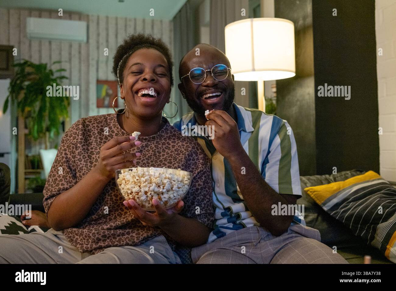 Happy African couple eating popcorn during watching the comedy and ...