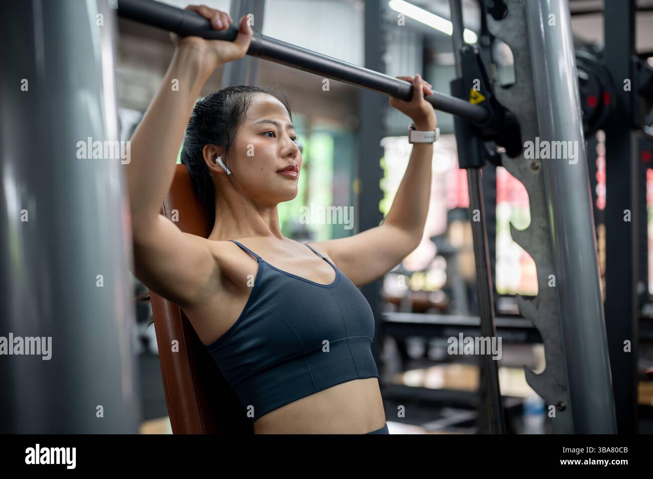 Asian woman in sportswear is lifting a barbell on an incline bench ...